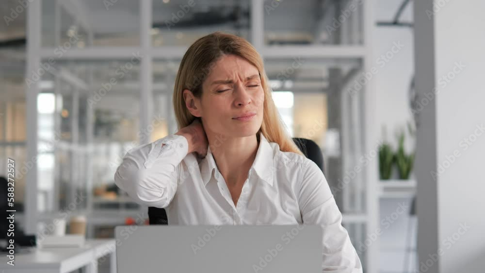 Tired businesswoman is experiencing neck pain while working in office ...