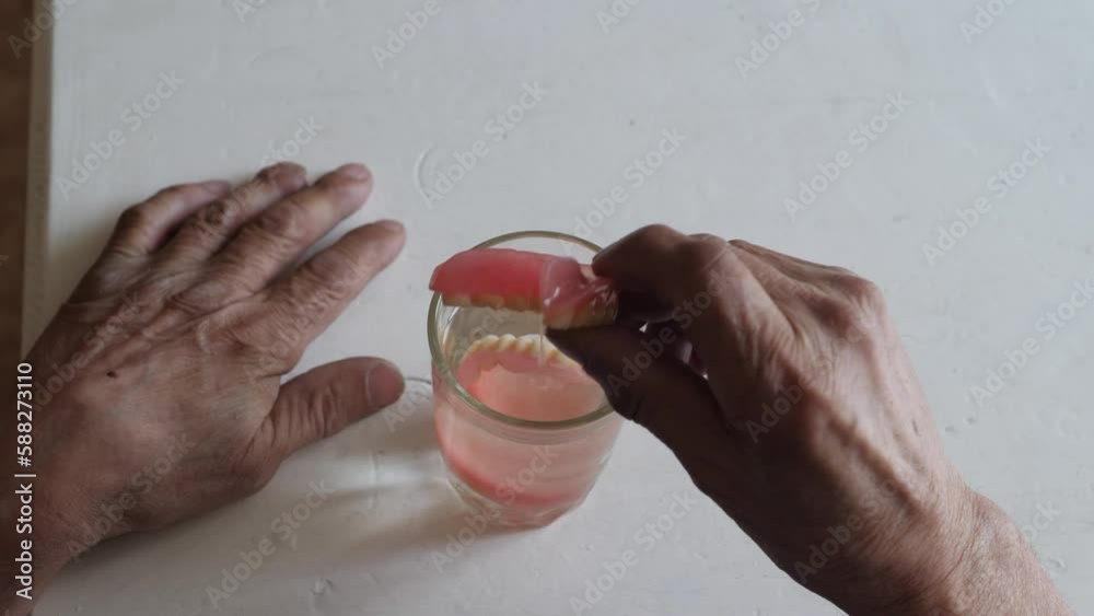 an elderly man takes out dentures from a glass of water and puts them ...
