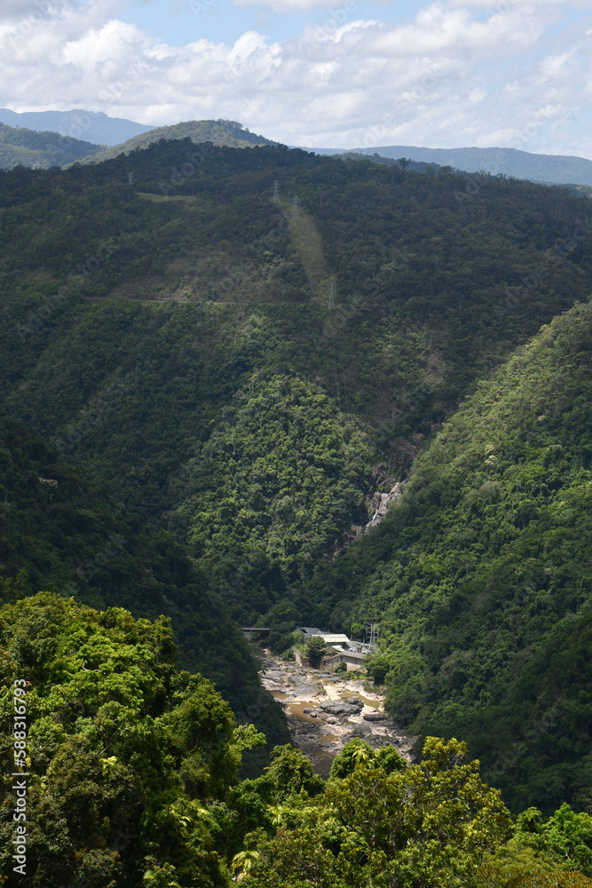 A clearing is visible in a steep valley of a rain forest. Wires stretch ...