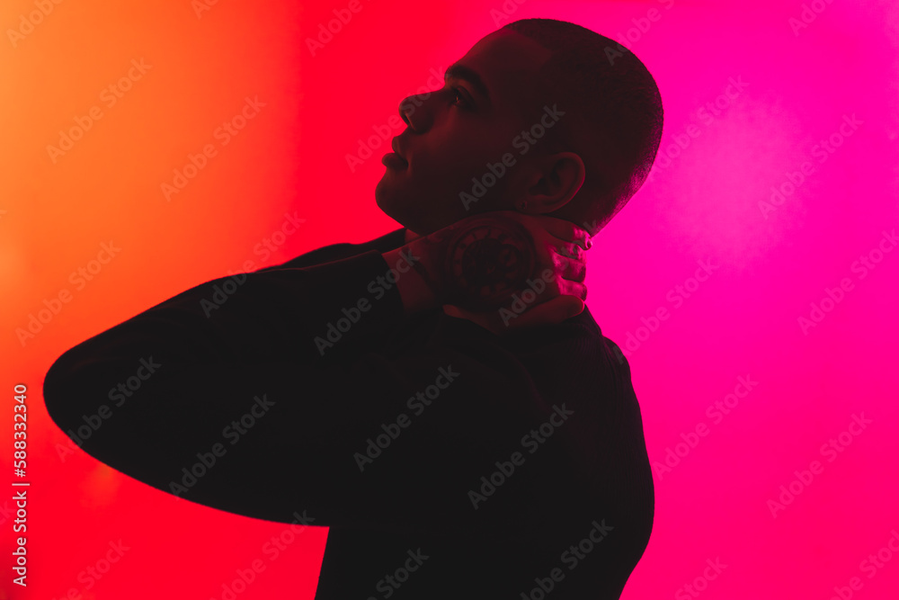 Stressed tattooed man standing sideways and touching back of his neck ...