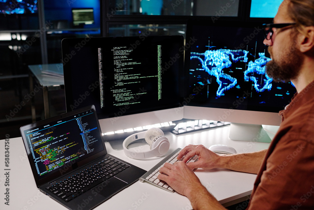 Close-up of young programmer or IT engineer typing on desktop computer keyboard while decoding ...