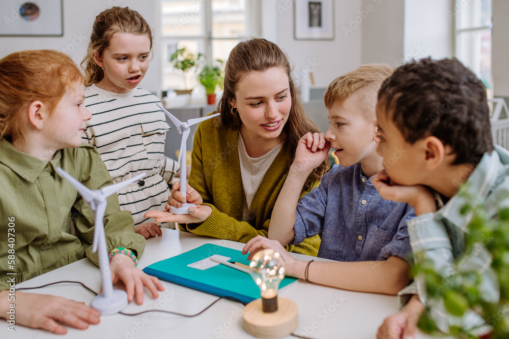 Young teacher with model of wind turbine learning pupils about wind ...