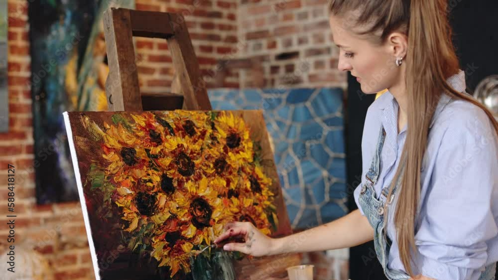 Young beautiful female artist painting still life with sunflower on ...