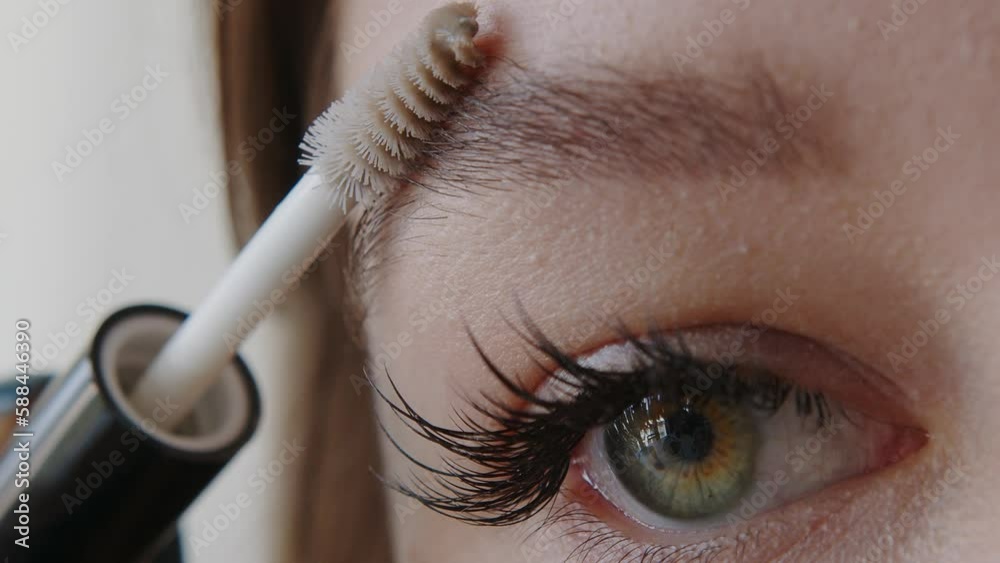 Young beautiful woman is combing and styling her eyebrows front of ...