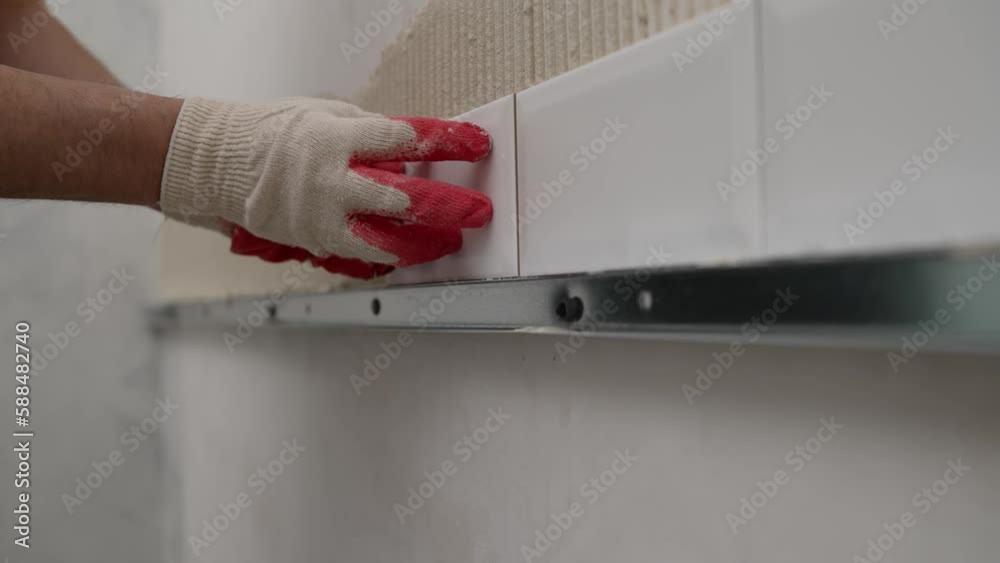 The hands of a handyman smear tile glue with a spatula on the wall next ...