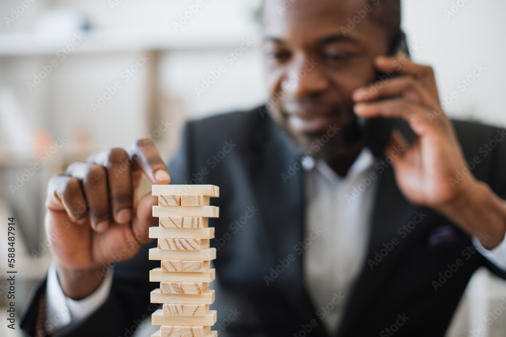 Happy multicultural man in business suit playing jenga while talking on ...
