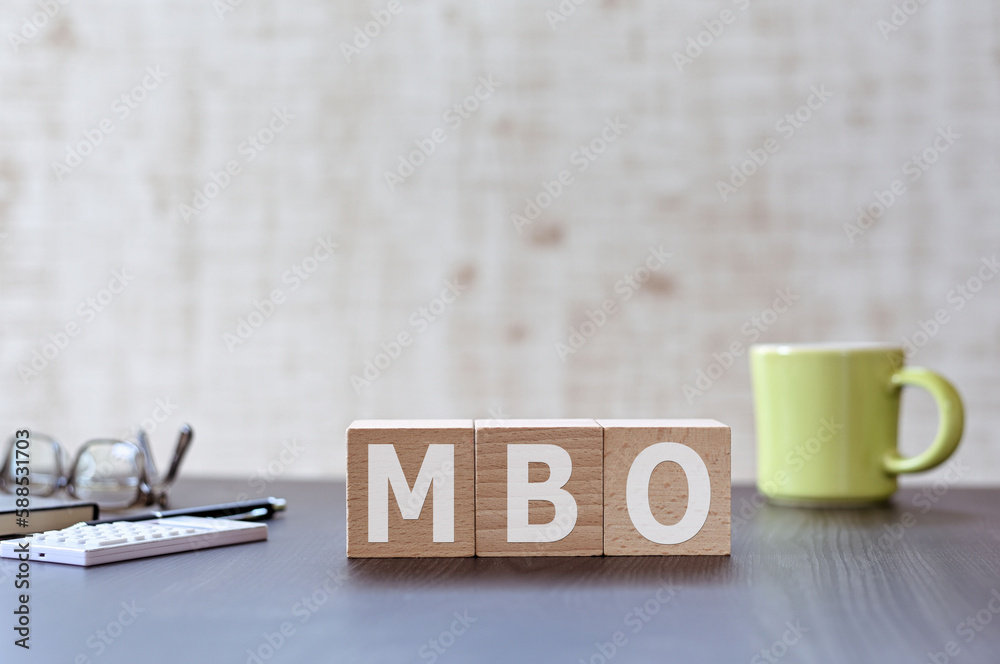 There is wood cube with the word MBO. It is an acronym for Management by Objectives an eye ...