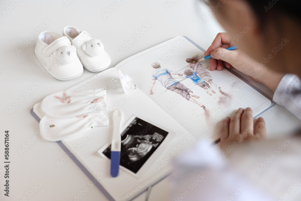 A pregnant woman is sketching the image of her family in a notebook ...