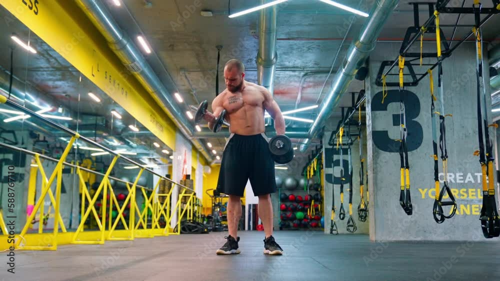 Bald bodybuilder exercising in the gym. Raises the barbell, dumbbells ...