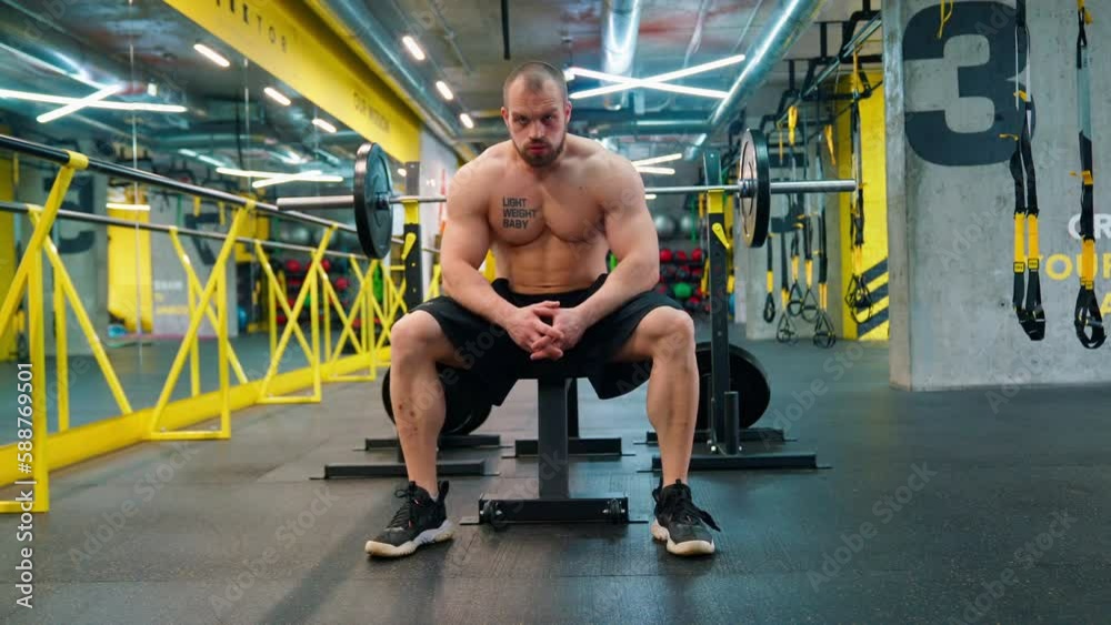 Bald bodybuilder exercising in the gym. Raises the barbell, dumbbells ...