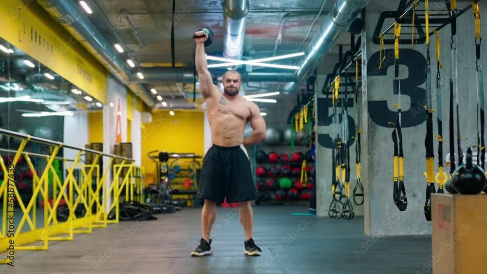 Bald bodybuilder exercising in the gym. Raises the barbell, dumbbells ...