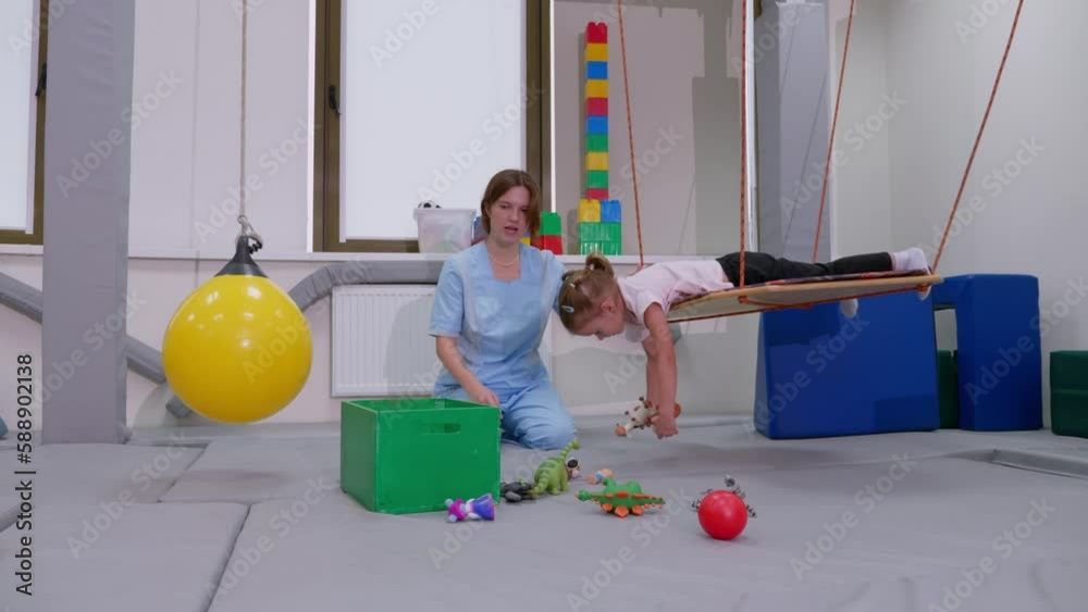 Child with physiotherapist on swing in sensory integration room. Little ...