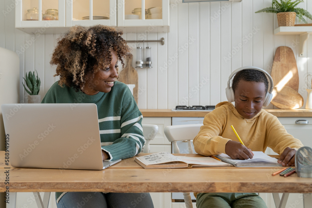 Smiling young African American mother doing homework with small son ...