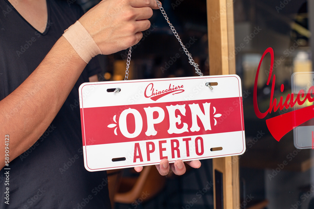 Foto de Man hanging up an Open sign on a restaurant door. Dual language ...