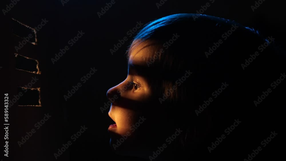 little girl trying to see something through a crack in a door or wall ...