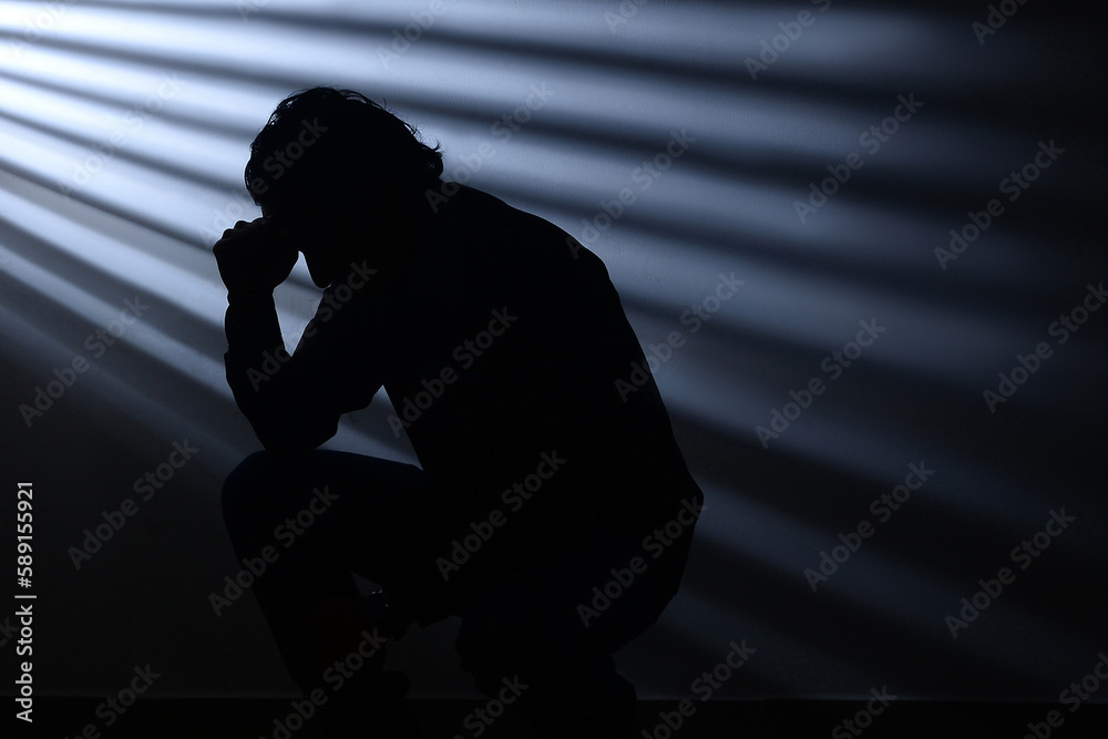 Silhouette of a desolate man bent over on his feet against a background ...