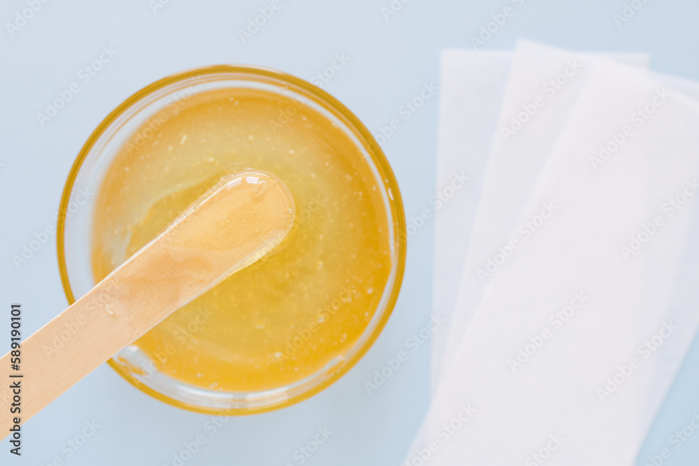 Liquid yellow sugar paste, wooden spatula, depilatory strips on a blue ...
