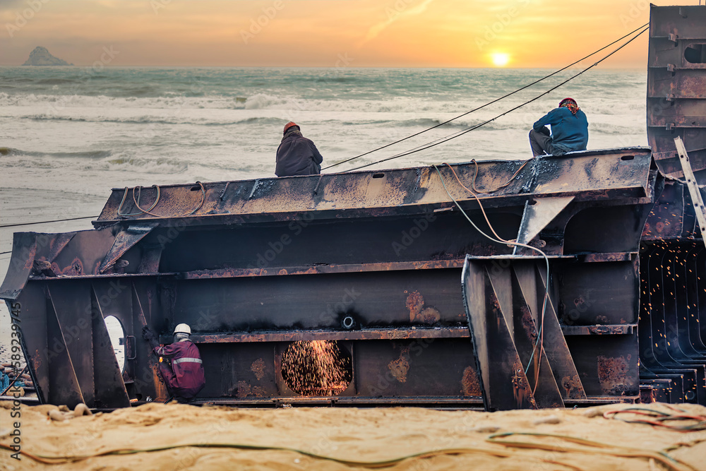 Shipbreaking of a large oil tanker in the harbor, labour cutting the ...