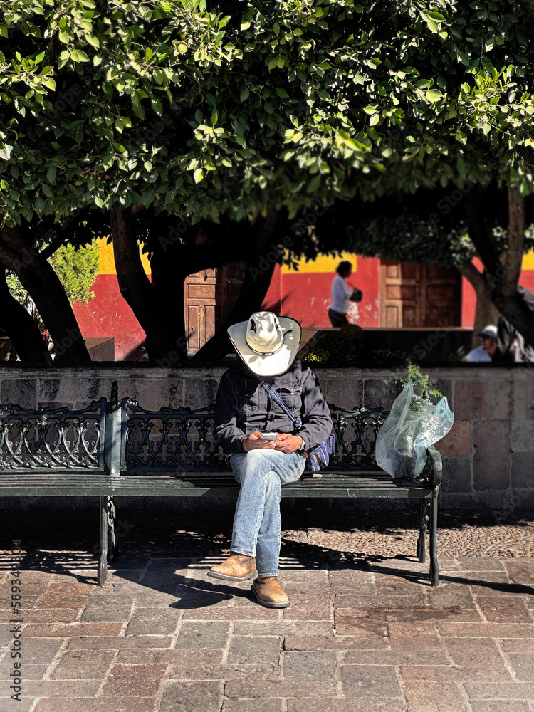 A Mexican man, his face hidden by a white stetson hat sitting on a ...