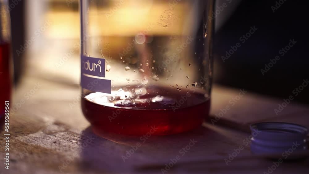 red liquid is poured into a beaker and stirred with a small wooden ...