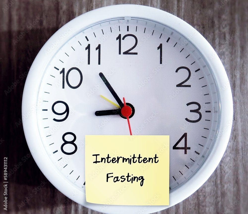 Wall clock with sticky note written INTERMITTEN FASTING, eating plan ...