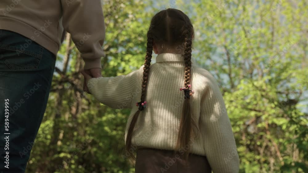 father leads child by hand outdoors. happy family park. dad daughter go ...