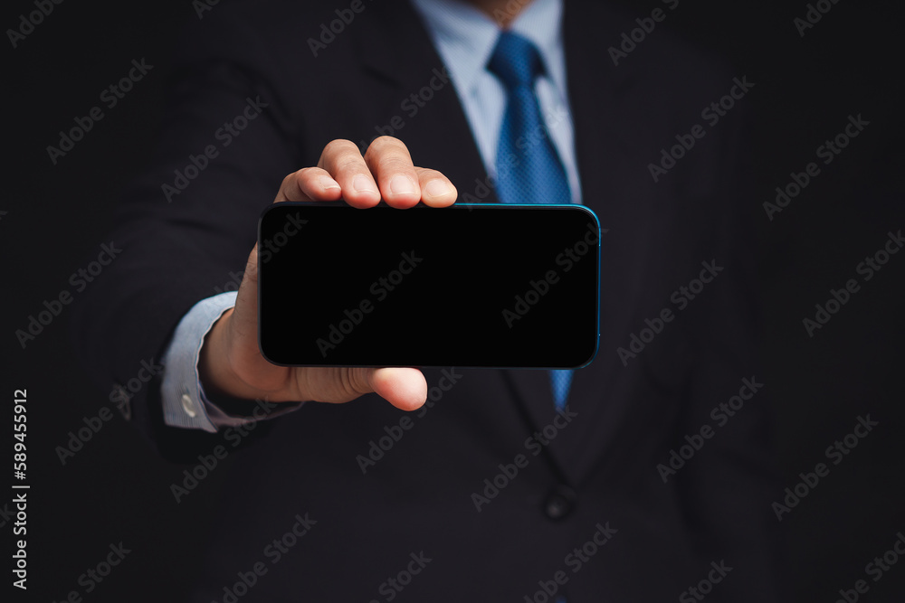 Hand holding a black blank screen smartphone against a black background ...