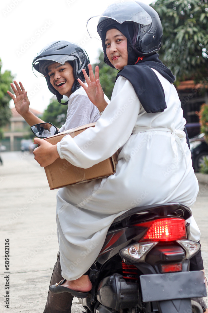 Muslim couple riding a motorcycle wearing helmet, looking back and ...