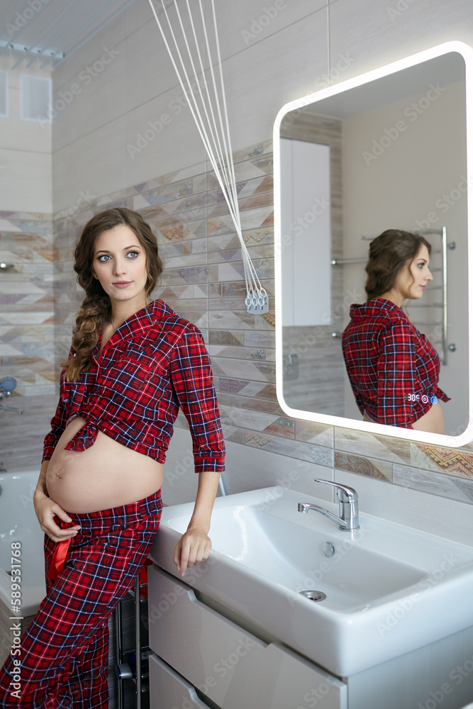 Foto de A pregnant woman in the bathroom. Female dressed in red pajama ...
