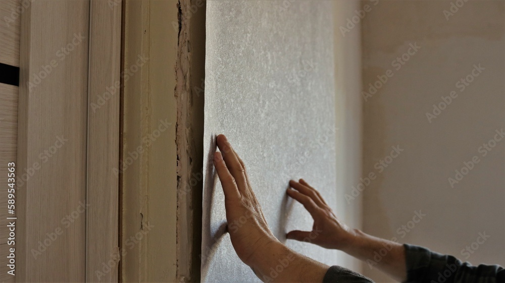 male hands sticking a strip of gray wallpaper on the wall in the room ...