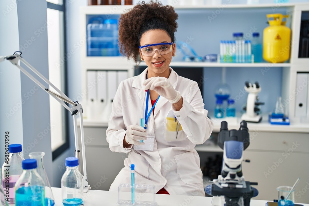 Young african american woman wearing scientist uniform using pipette ...