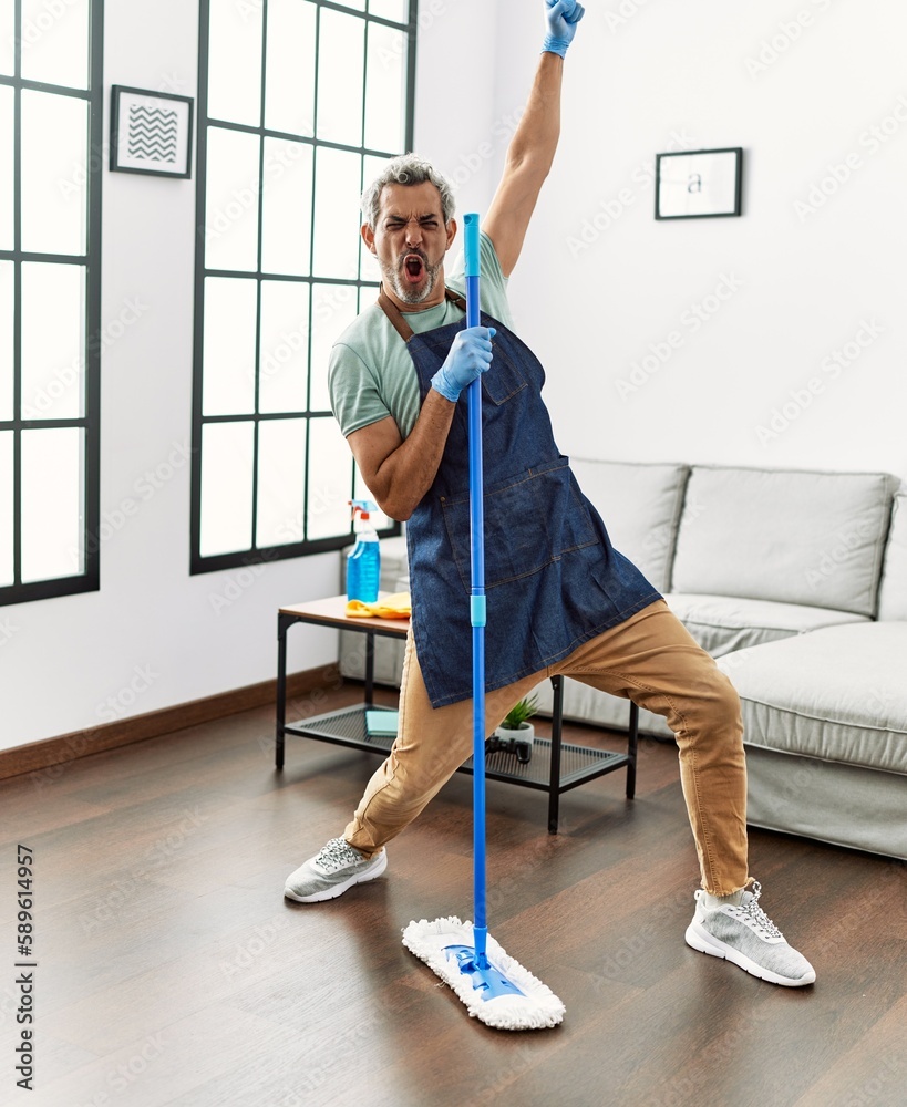 Middle age grey-haired man singing song using mop as a microphone at ...