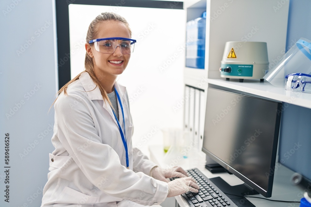 Young blonde woman wearing scientist uniform using computer working at ...