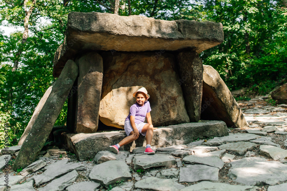Foto de Little girl sit near ancient dolmen and rest in green park ...