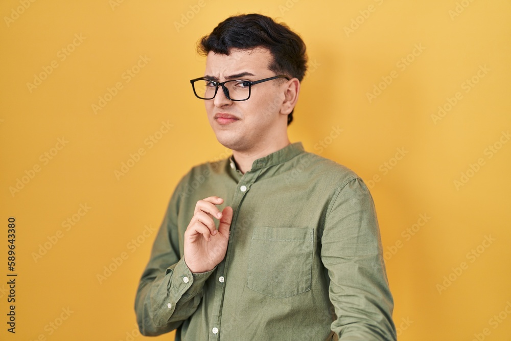 Non binary person standing over yellow background disgusted expression ...