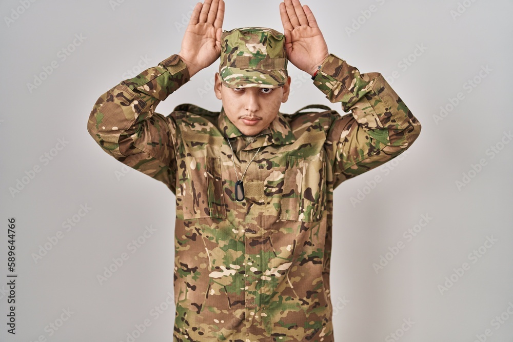 Young arab man wearing camouflage army uniform doing bunny ears gesture ...