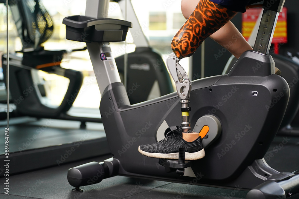 Young female with one prosthetic leg with exercising with a spinning ...