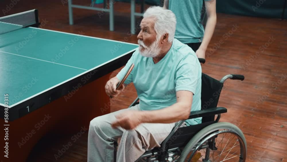 An elderly person with a disabilities in a wheelchair serves a ping ...