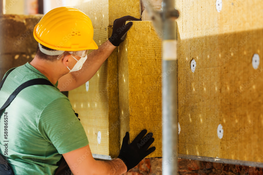 Construction worker insulates brick wall of house with mats of rock ...
