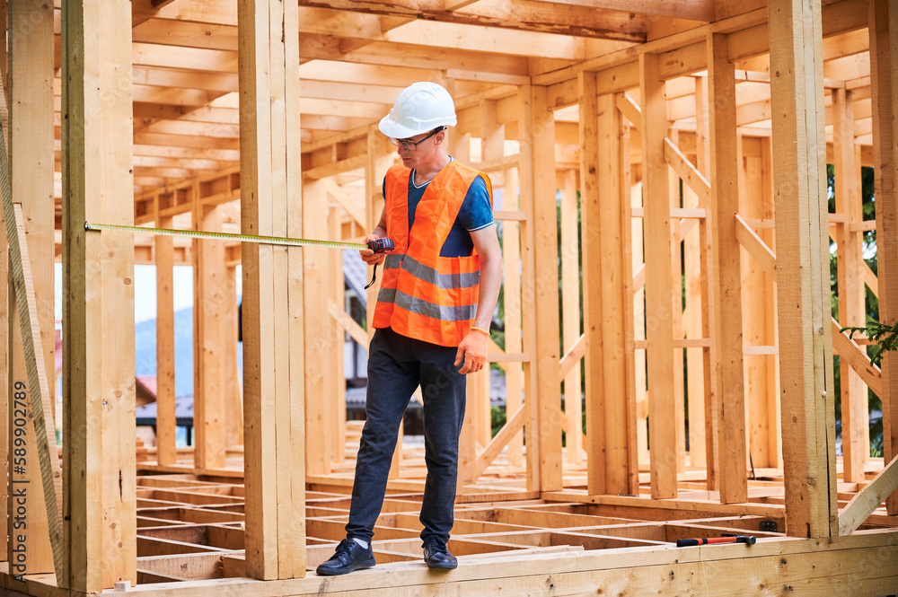Carpenter constructing wooden skeleton building. Man measures distances ...
