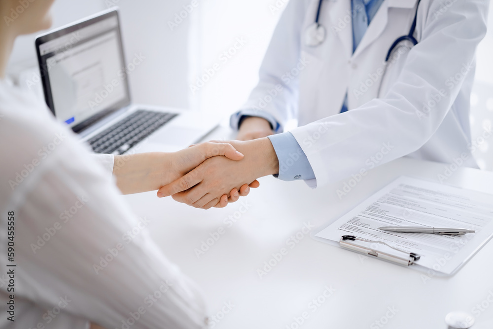 Doctor and patient shaking hands while sitting opposite of each other ...