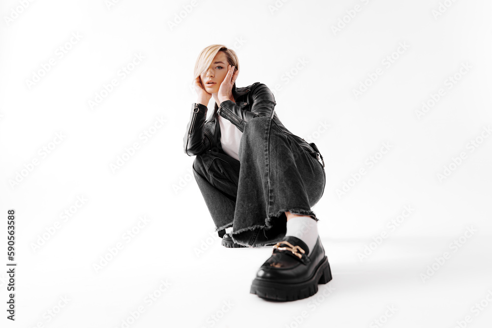 Full body of young female in leather jacket and boots sitting on ...