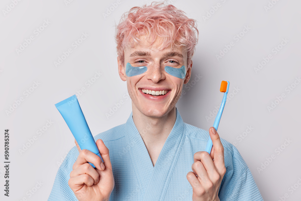 Portrait of cheerful man with pink curly hair holds tube of toothpaste ...