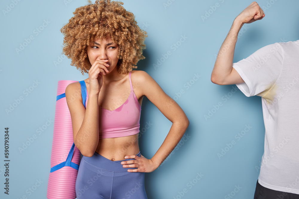 Displeased curly haired woman smells something stinky and disgusting ...