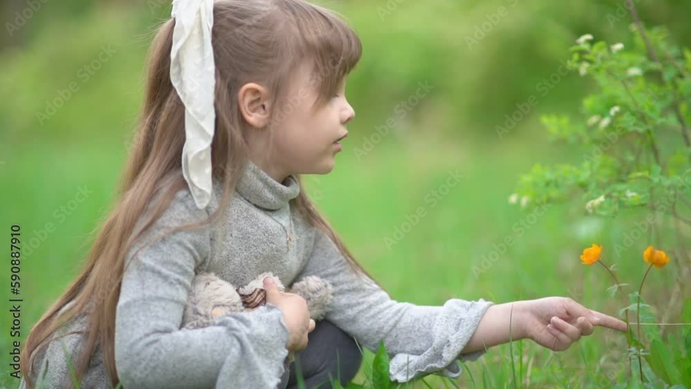 Little girl touch strokes orange flower in the park. Background summer ...