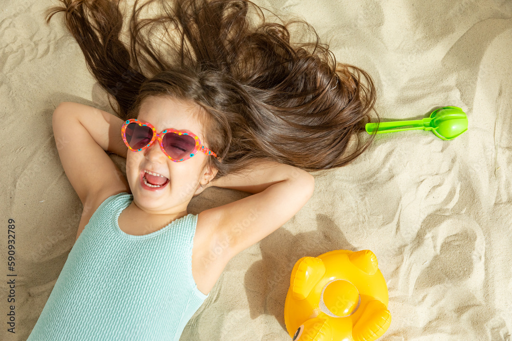 Foto de Happy little girl lying on a sandy beach and sunbathe in the ...