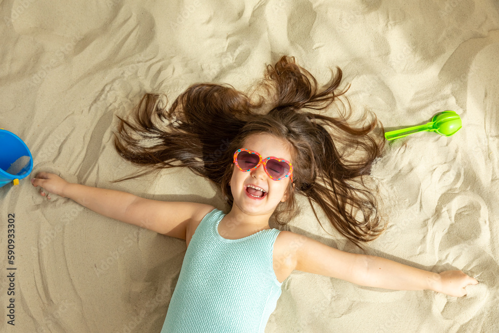 Foto de Happy cute little girl lying on a sandy beach and sunbathe in ...