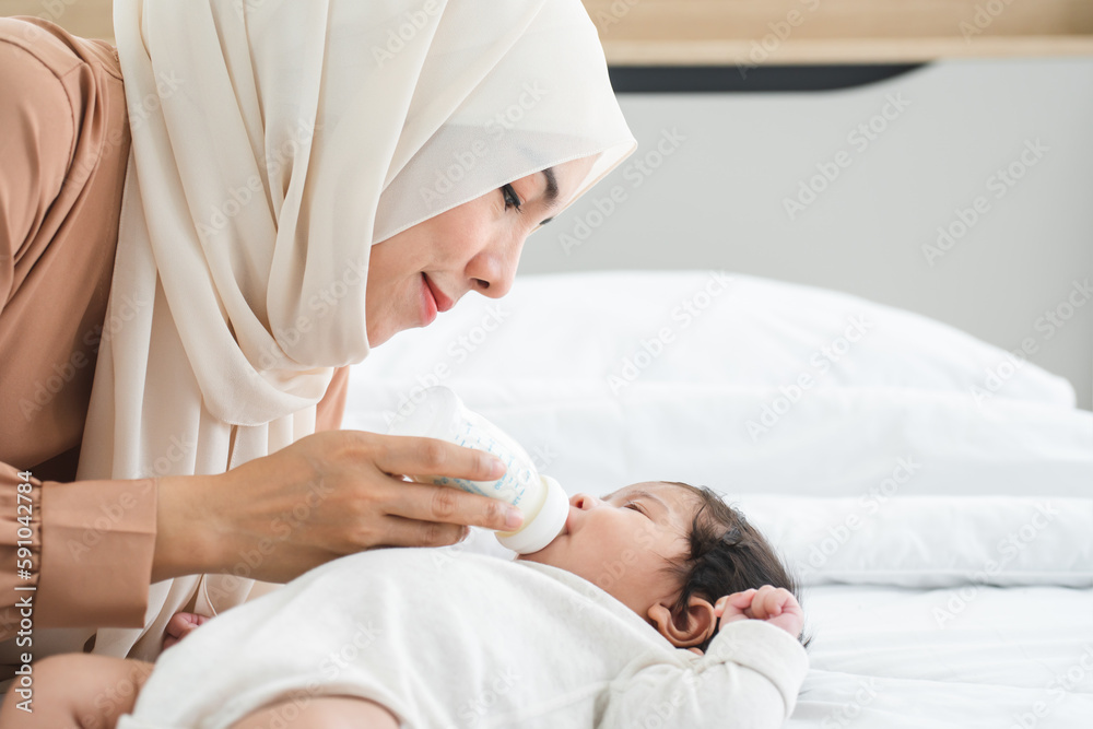 Happy Asian young Muslim mother wear hijab holding milk bottle, feeding ...