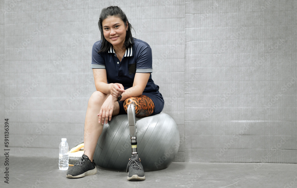 Asian woman with prosthetic leg sits isolated in gym. Young girl with ...