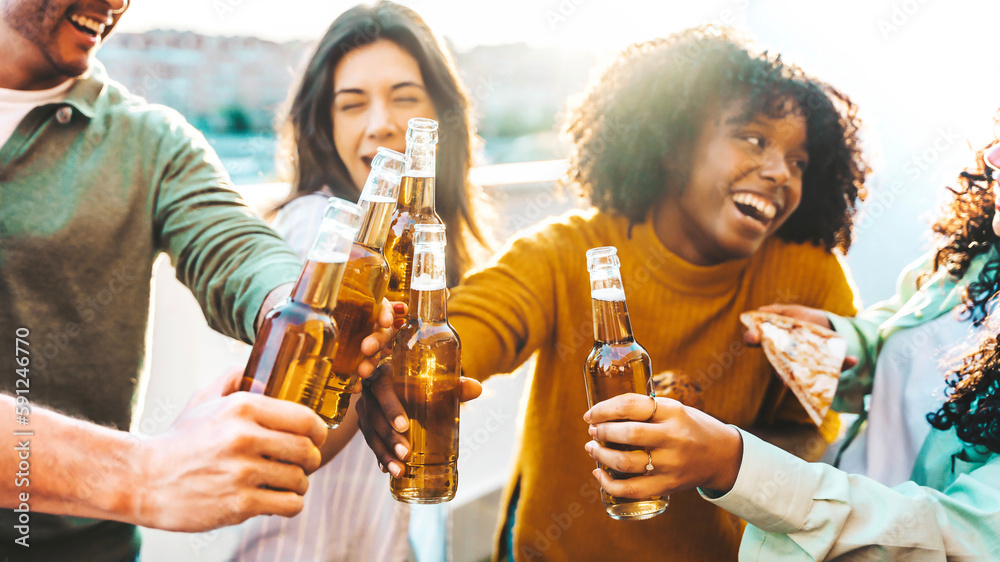 Multi ethnic friends cheering beer bottles at rooftop party event ...